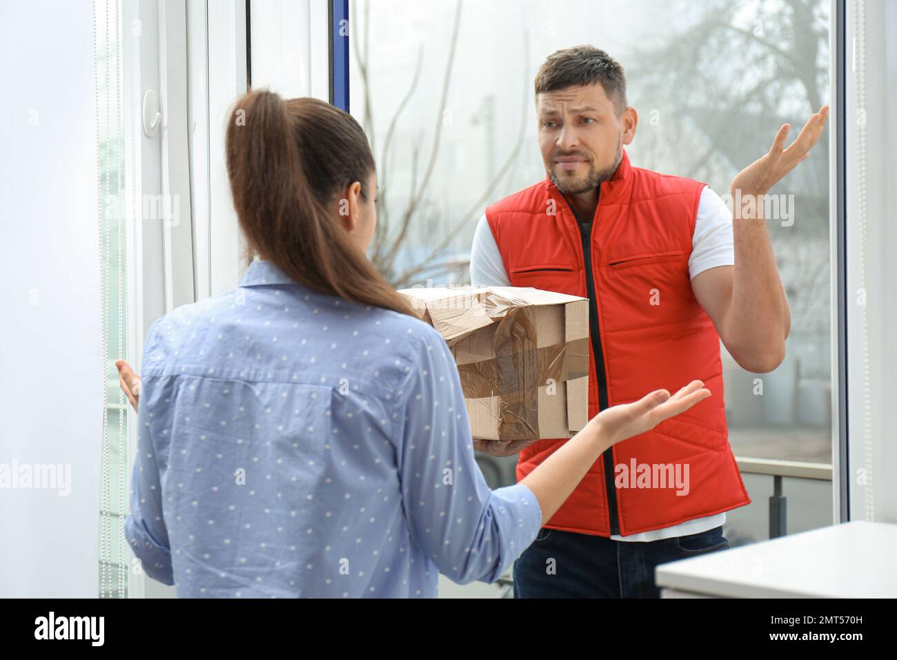 Emotional courier giving damaged cardboard box to client in doorway ...