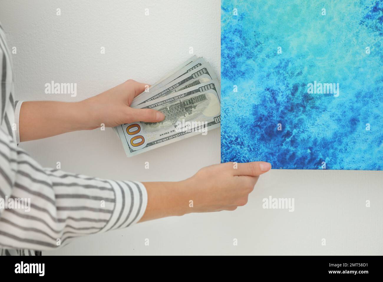 Woman hiding dollar banknotes behind painting indoors, closeup. Money ...