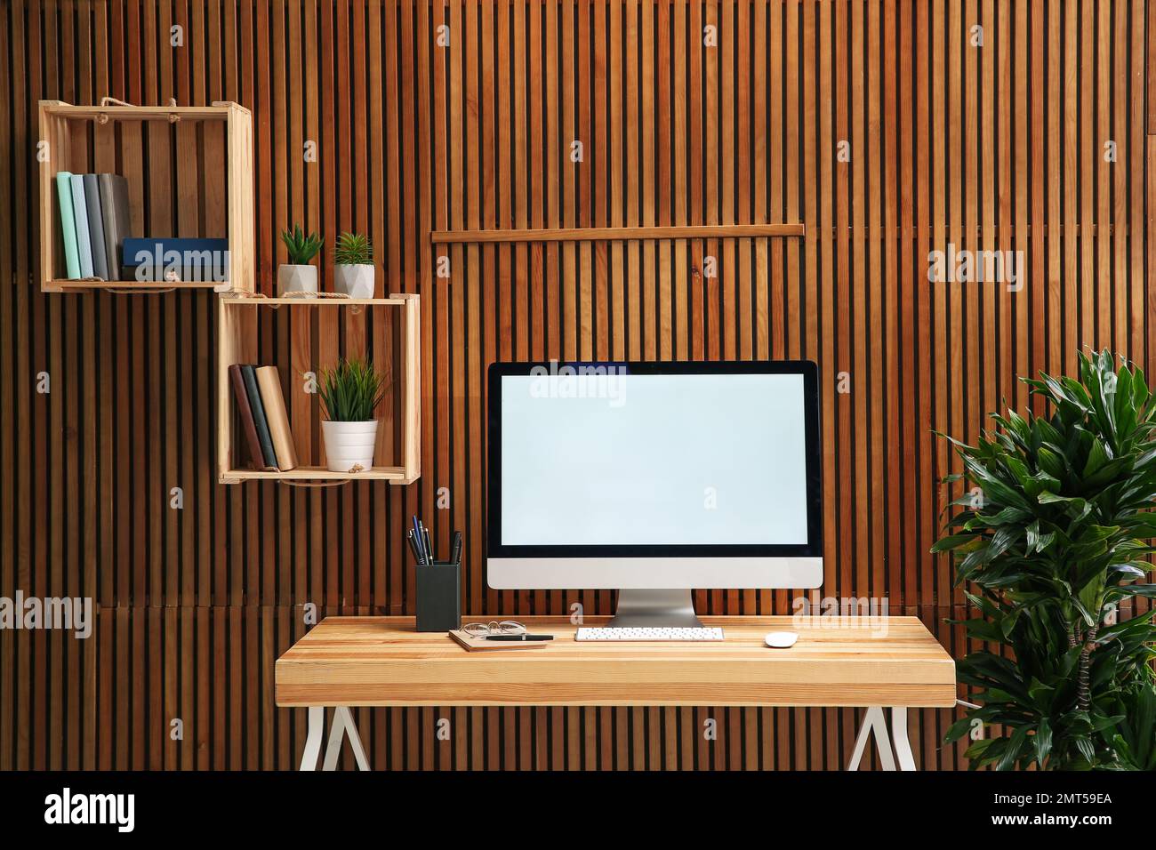 Comfortable workplace with computer near wooden wall in stylish room ...