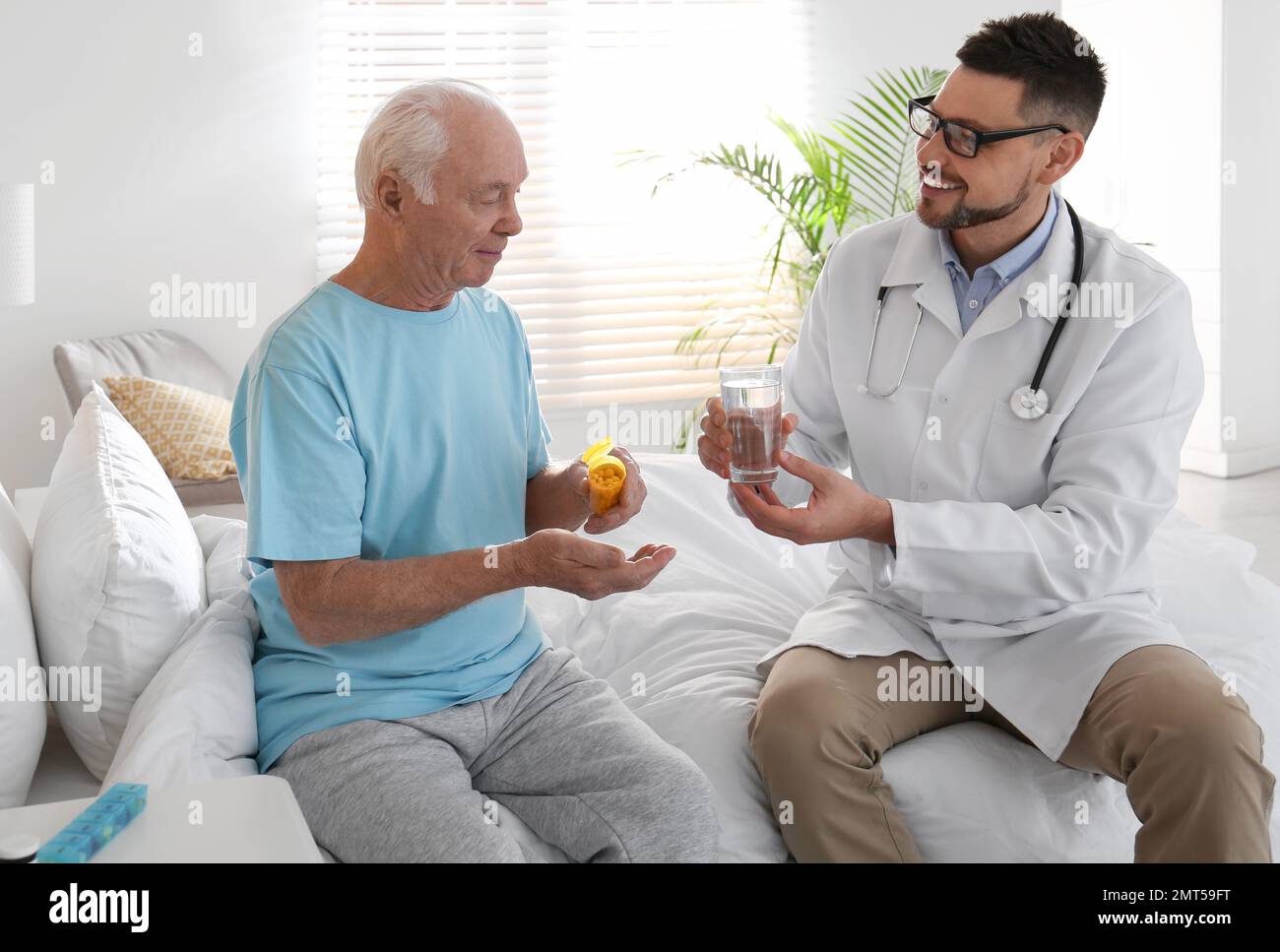 Doctor giving water to senior patient with pills in modern hospital ...