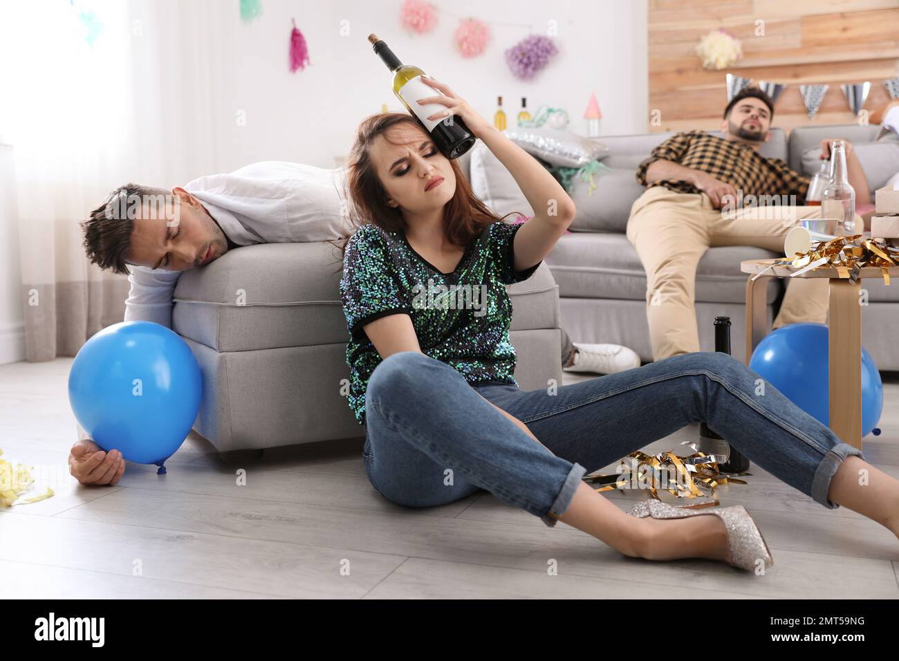 Young woman suffering from hangover and her friend sleeping in messy ...