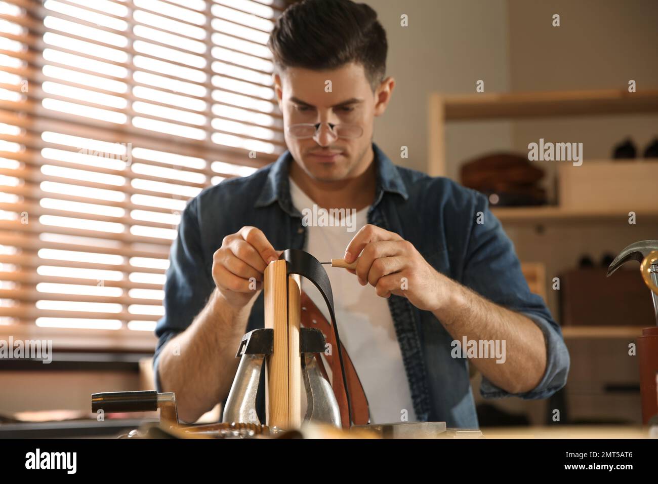 Man making holes in leather belt with stitching awl at workshop Stock ...