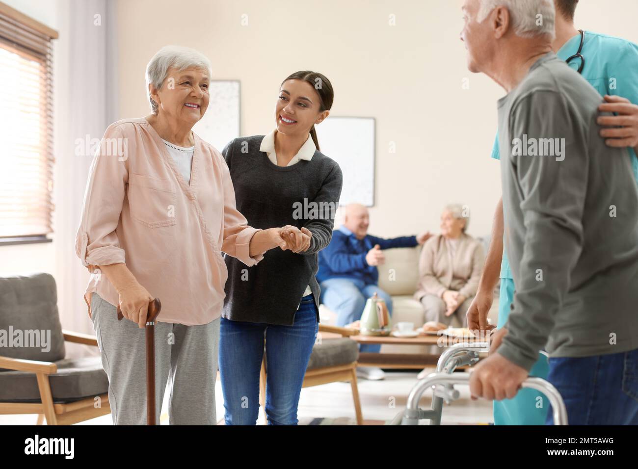 Care workers helping to elderly patients to walk in geriatric hospice ...