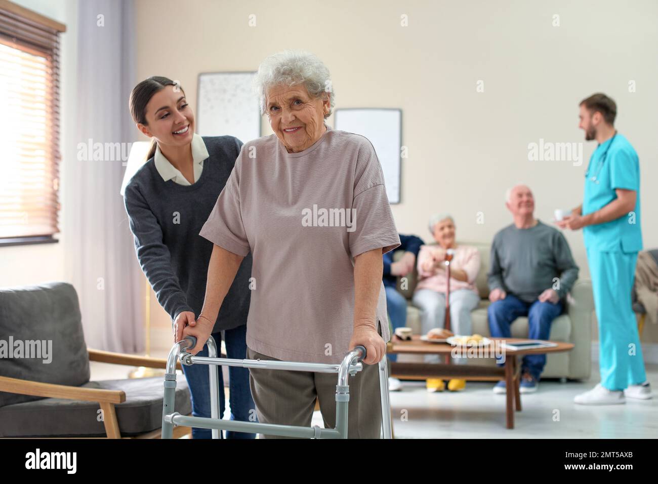 Care worker helping to elderly woman with walker in geriatric hospice ...