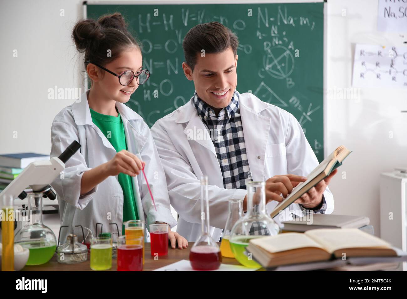 Teacher with pupil making experiment at table in chemistry class Stock ...