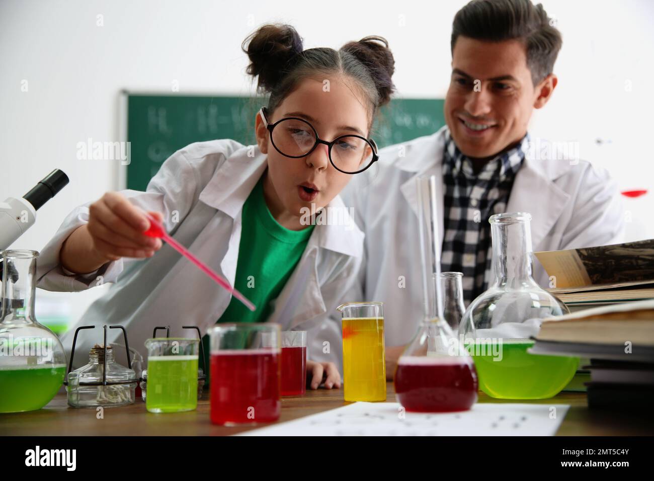 Teacher with pupil making experiment at table in chemistry class Stock ...