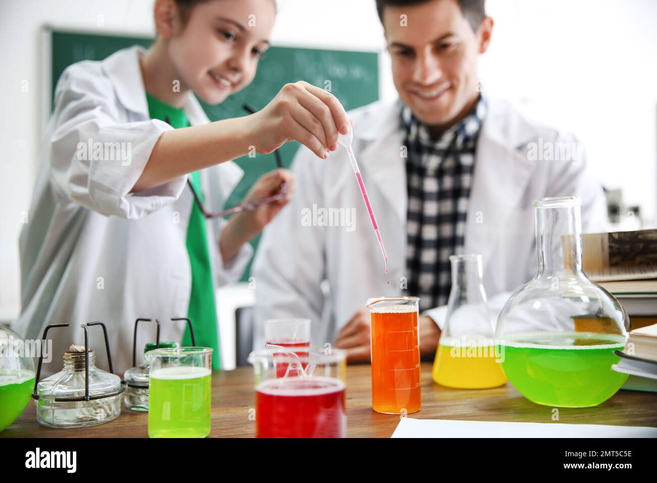 Teacher with pupil making experiment at table in chemistry class, focus ...