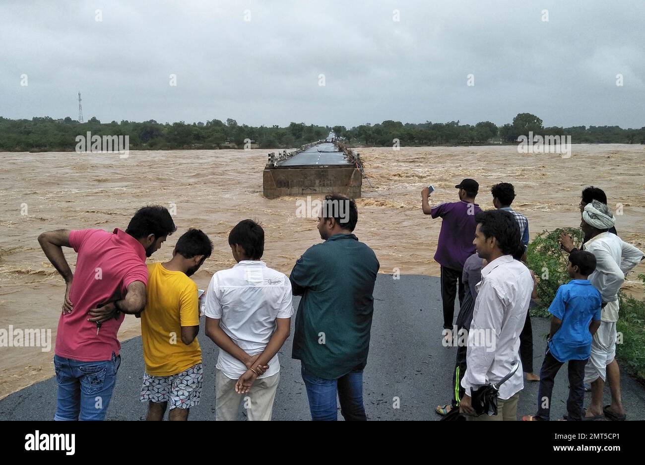 People watch after a bridge on the Deesa Dhanera highway was washed ...