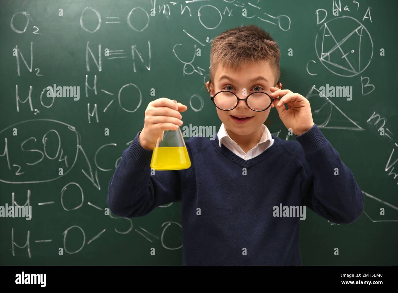 Schoolboy holding flask near chalkboard with chemical formulas Stock ...