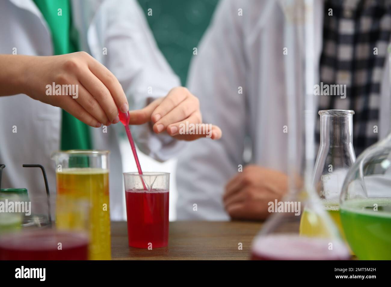 Teacher with pupil making experiment at table in chemistry class, focus ...