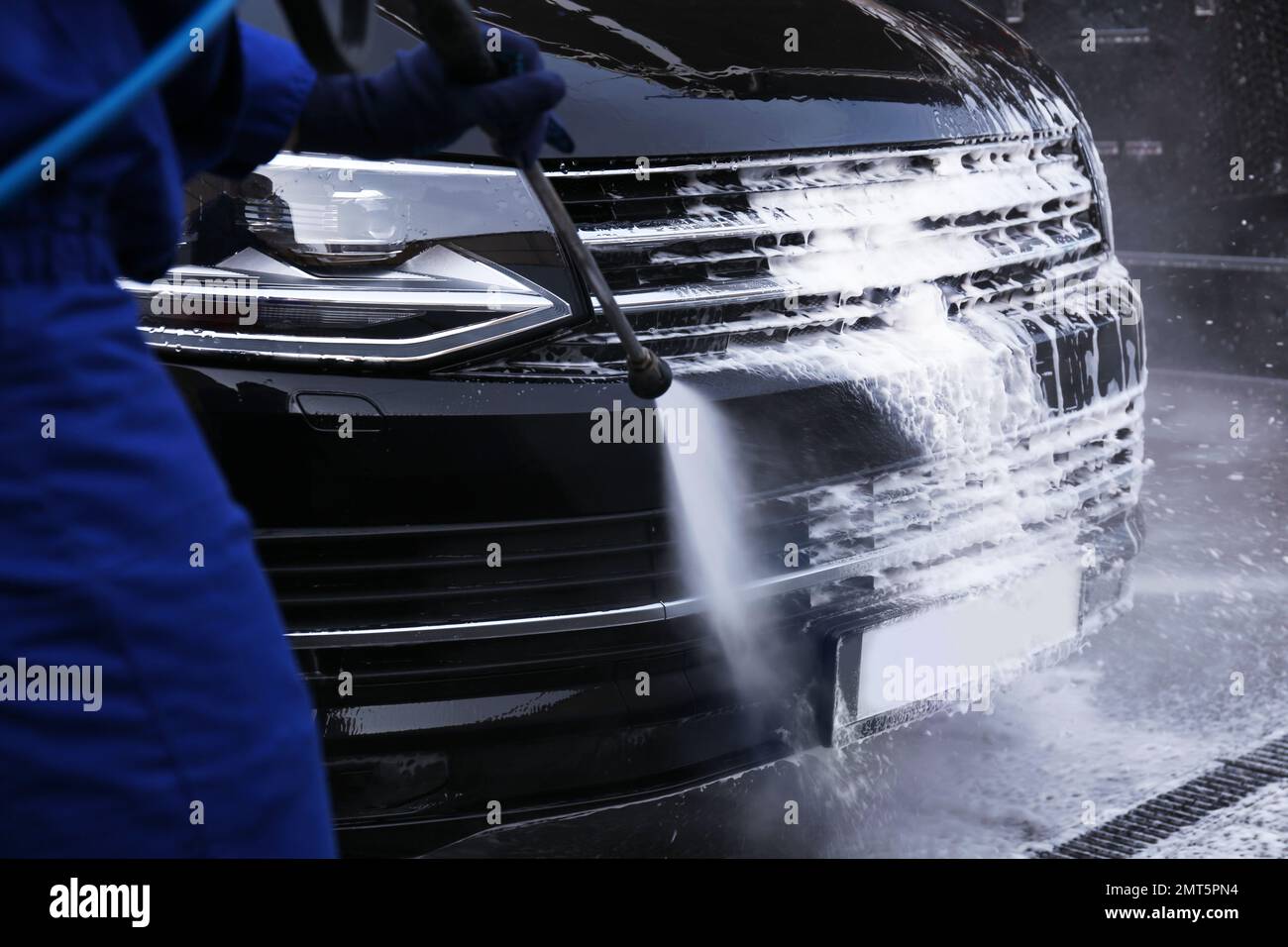 Worker cleaning automobile with high pressure water jet at car wash ...