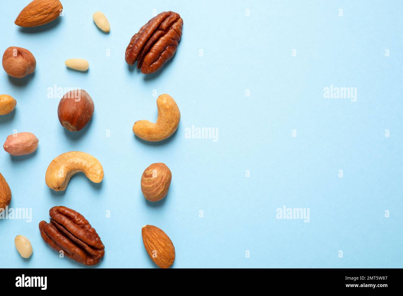 Different delicious nuts on light blue background, flat lay. Space for ...