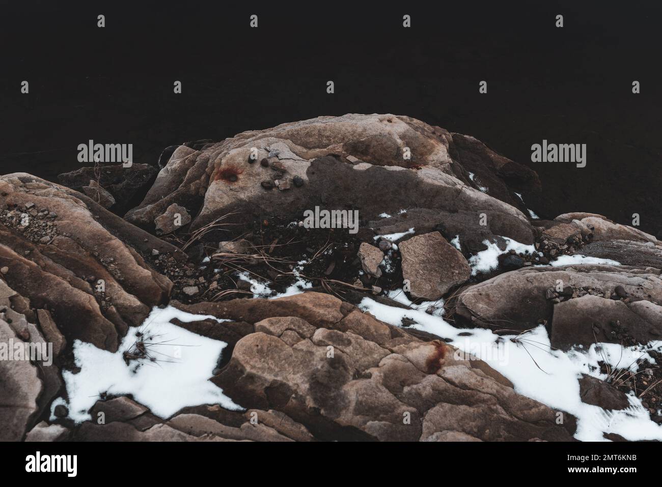 Outcrop of rock on the shore with snow and traces of rust from stones ...