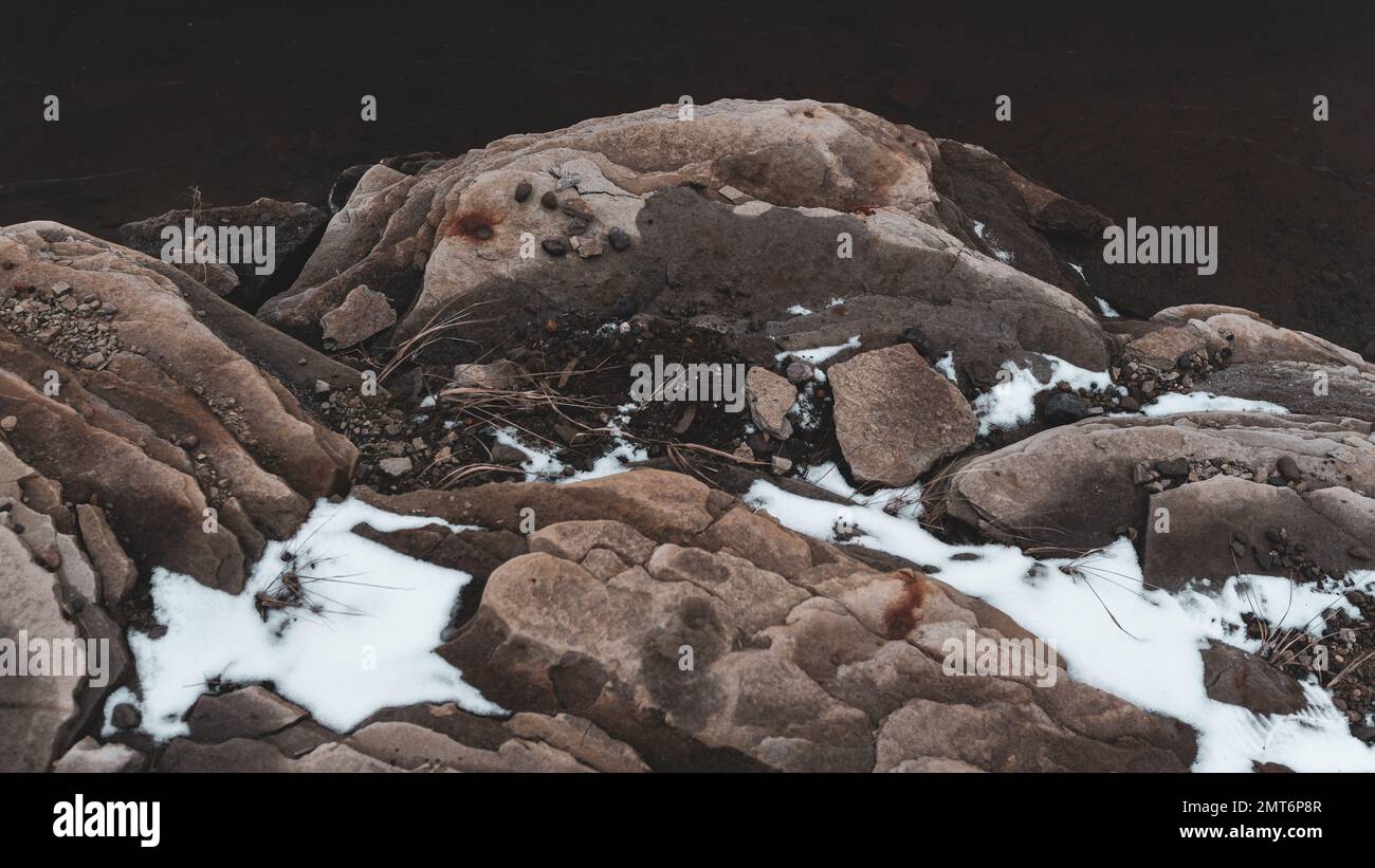 Photo of a rock outcrop on the shore with dark water with snow Stock ...