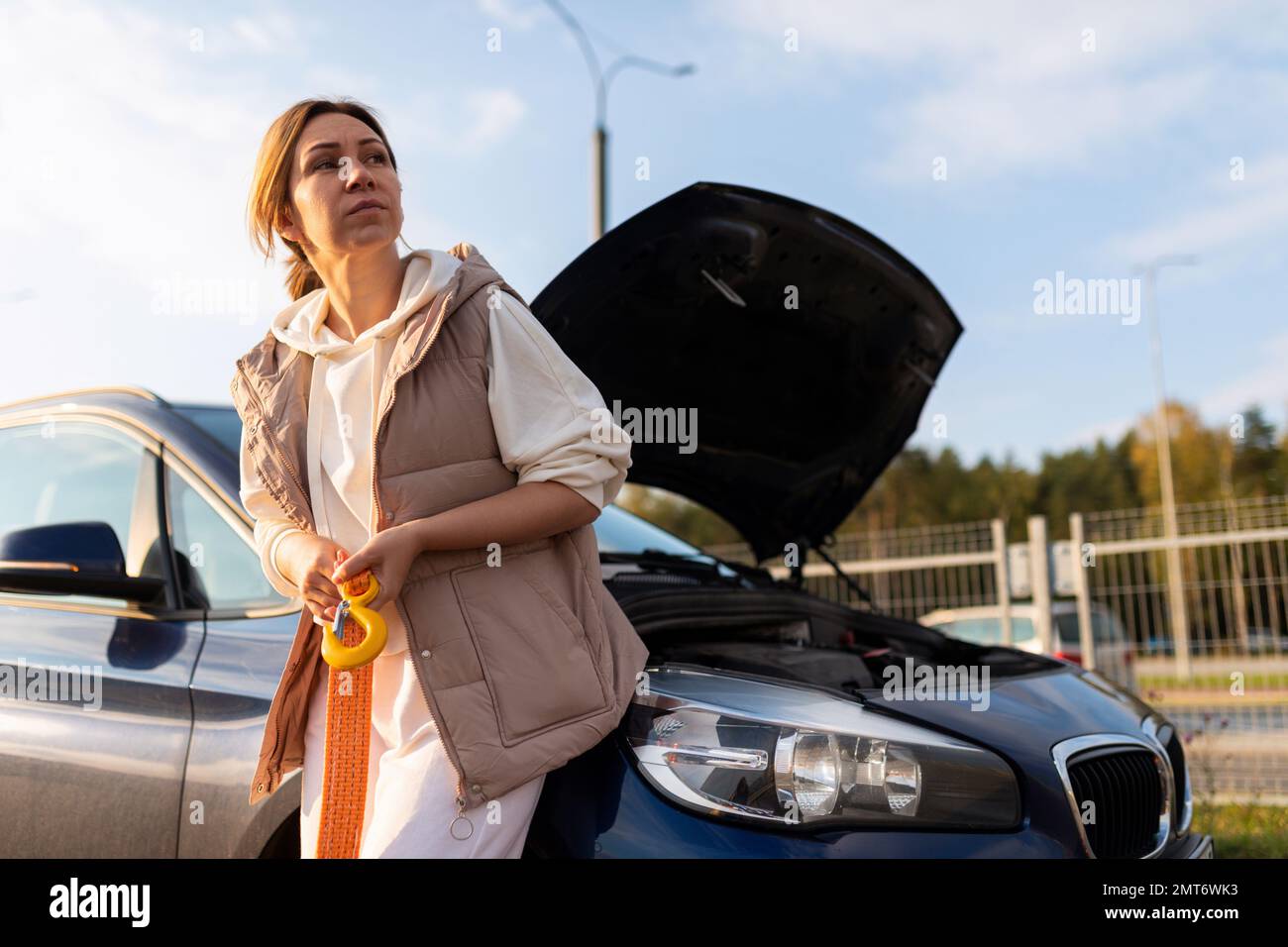 a woman in demand for towing stands near a broken down car with an open ...