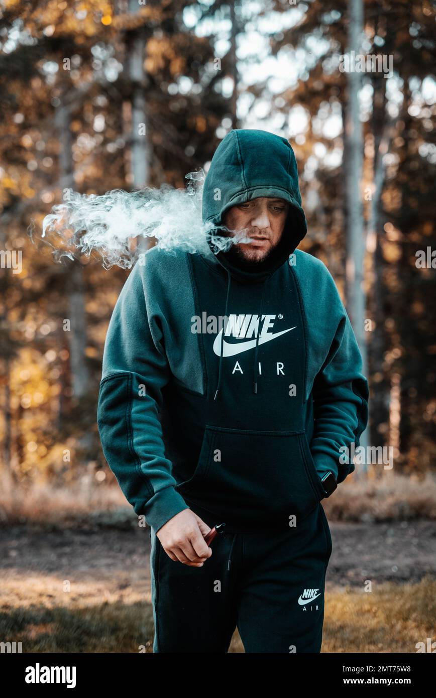 A caucasian guy smoking vape in the morning, yellow trees blurred ...