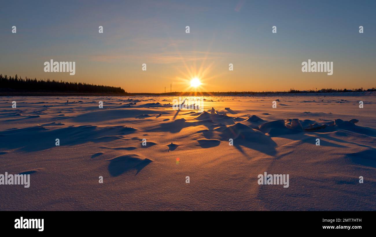 The bright sun at sunset shines on the ice on the Vilyui River in ...