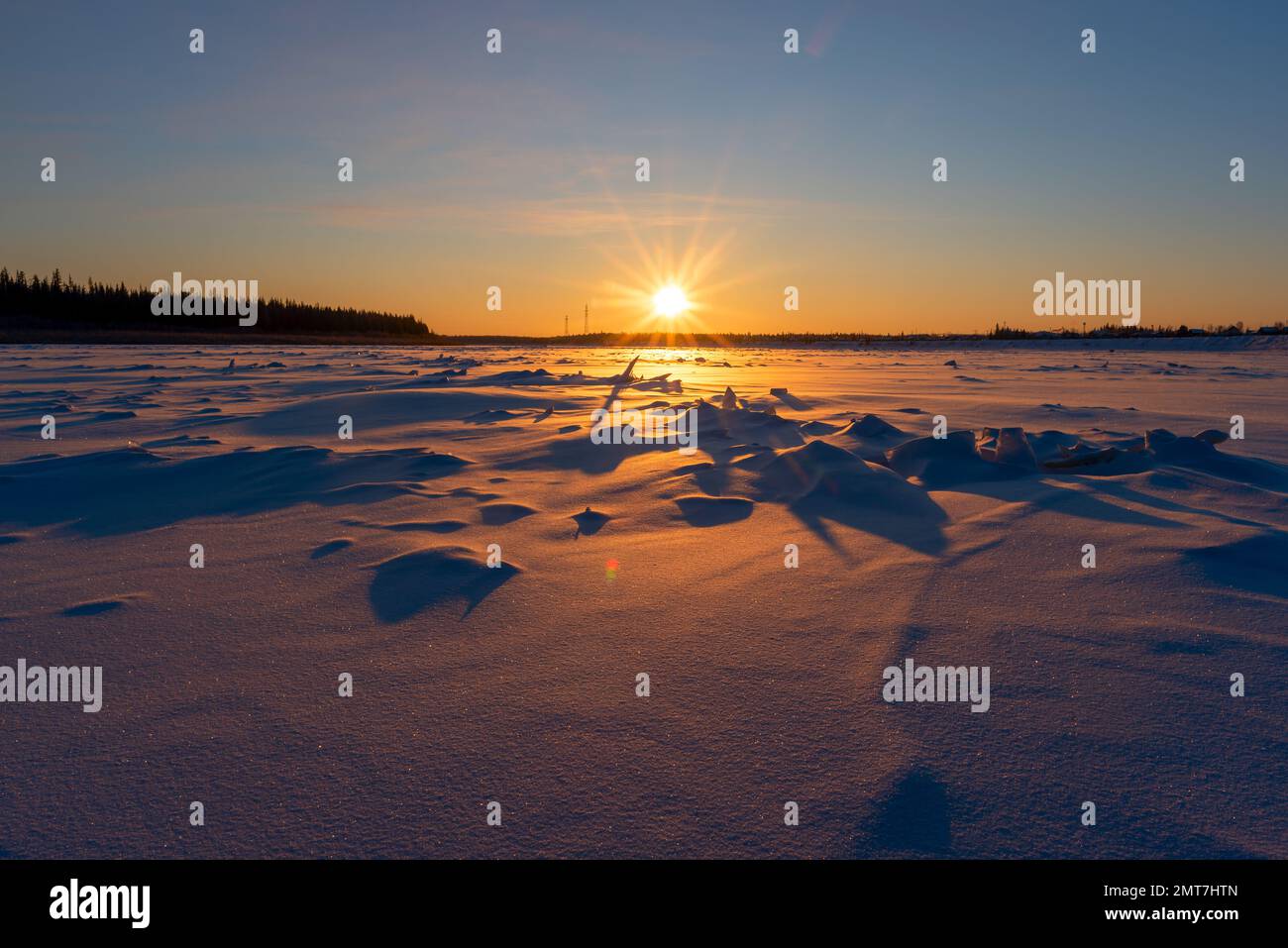 The bright sun at sunset sets behind a forest on the Vilyui River in ...