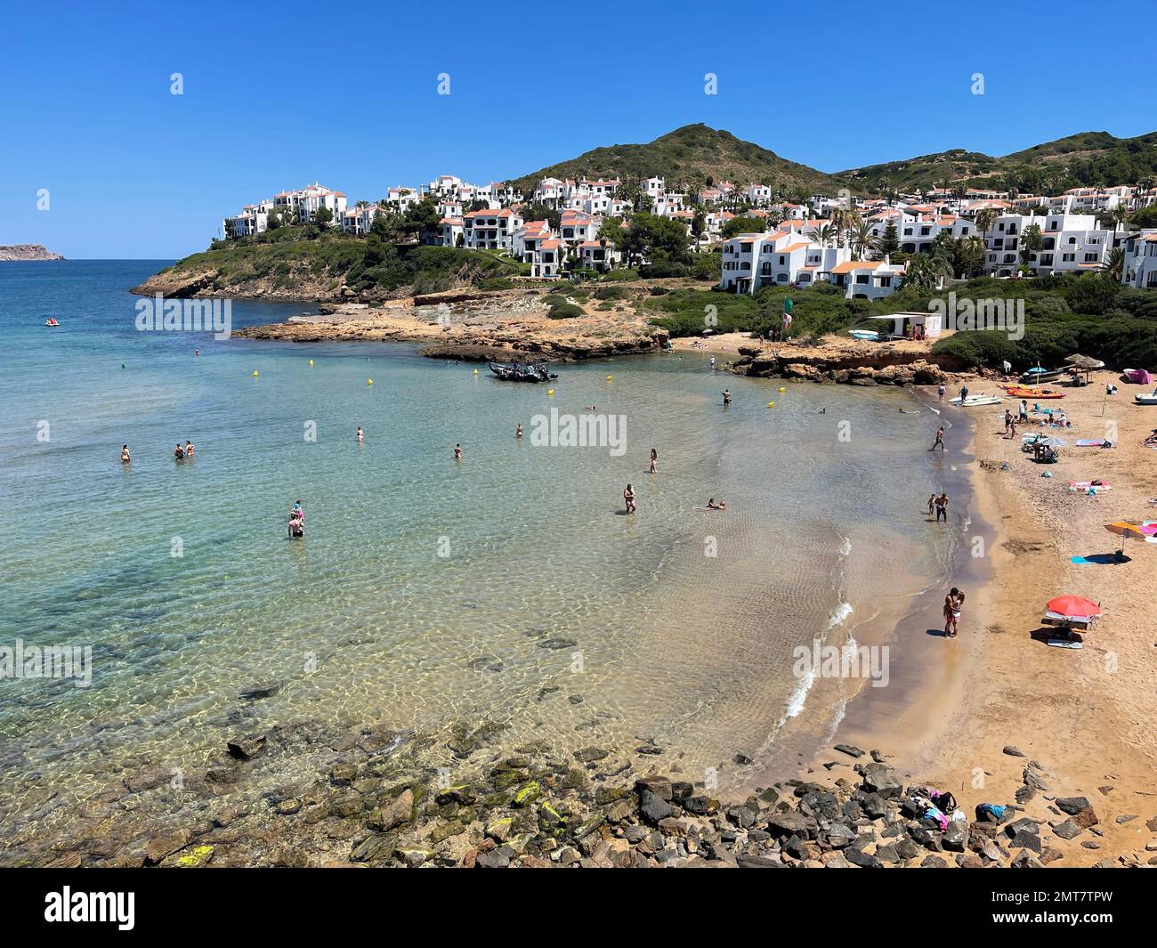 An aerial shot of people at the Fornells beach with white houses in the ...