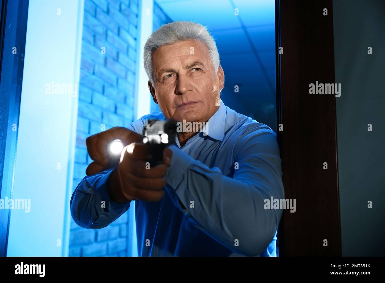 Professional security guard with gun and flashlight checking dark room ...