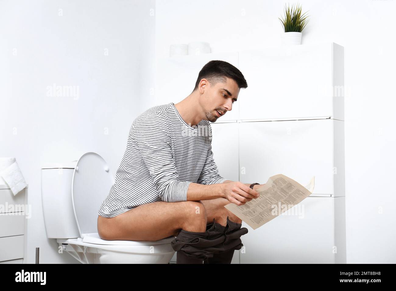 Man with newspaper sitting on toilet bowl in bathroom Stock Photo - Alamy