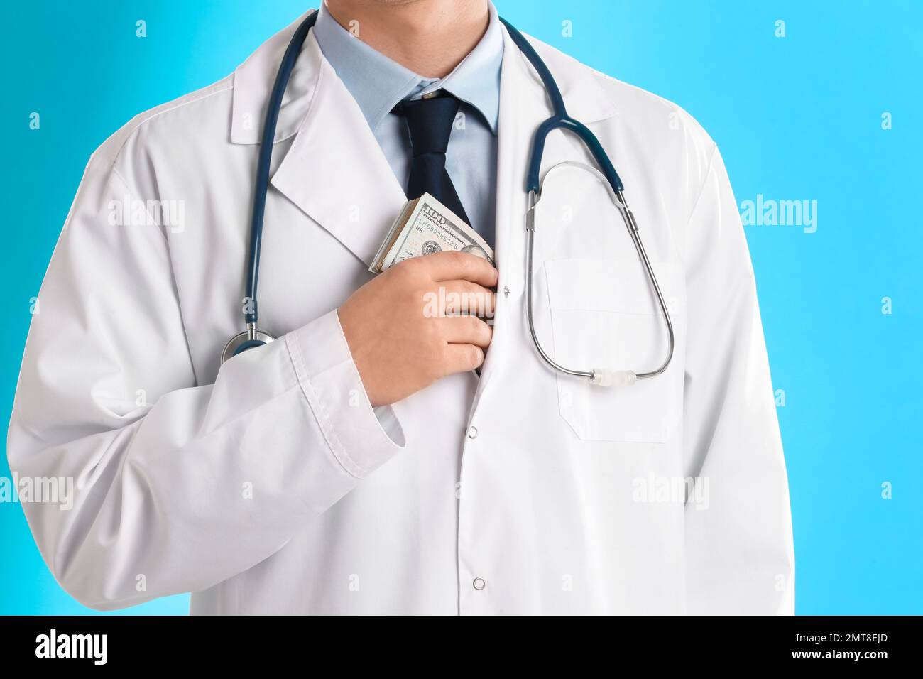 Doctor putting bribe into pocket on light blue background, closeup ...