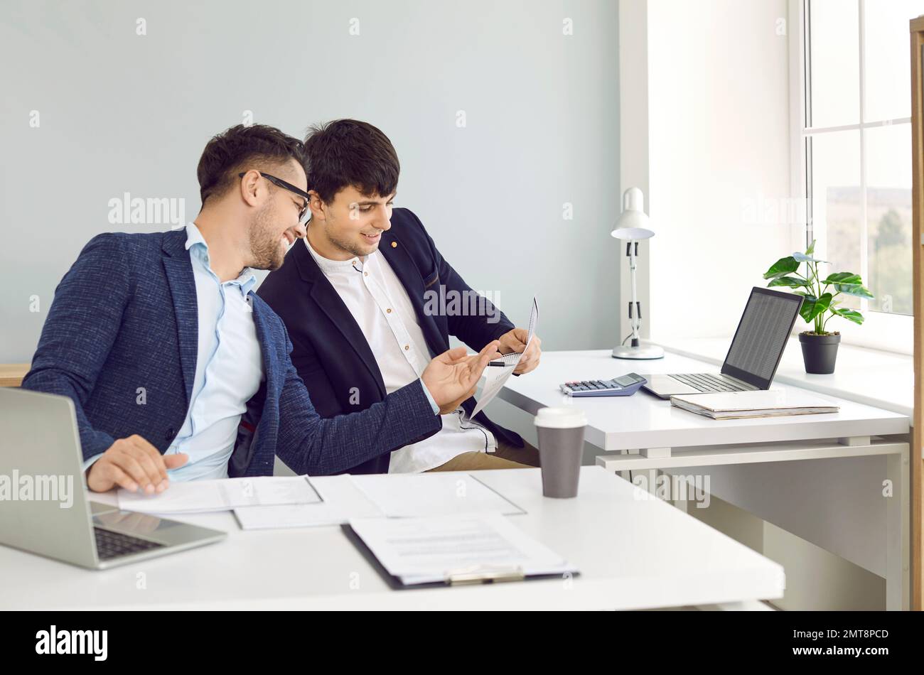 Two male office workers are reviewing documents together while sitting ...