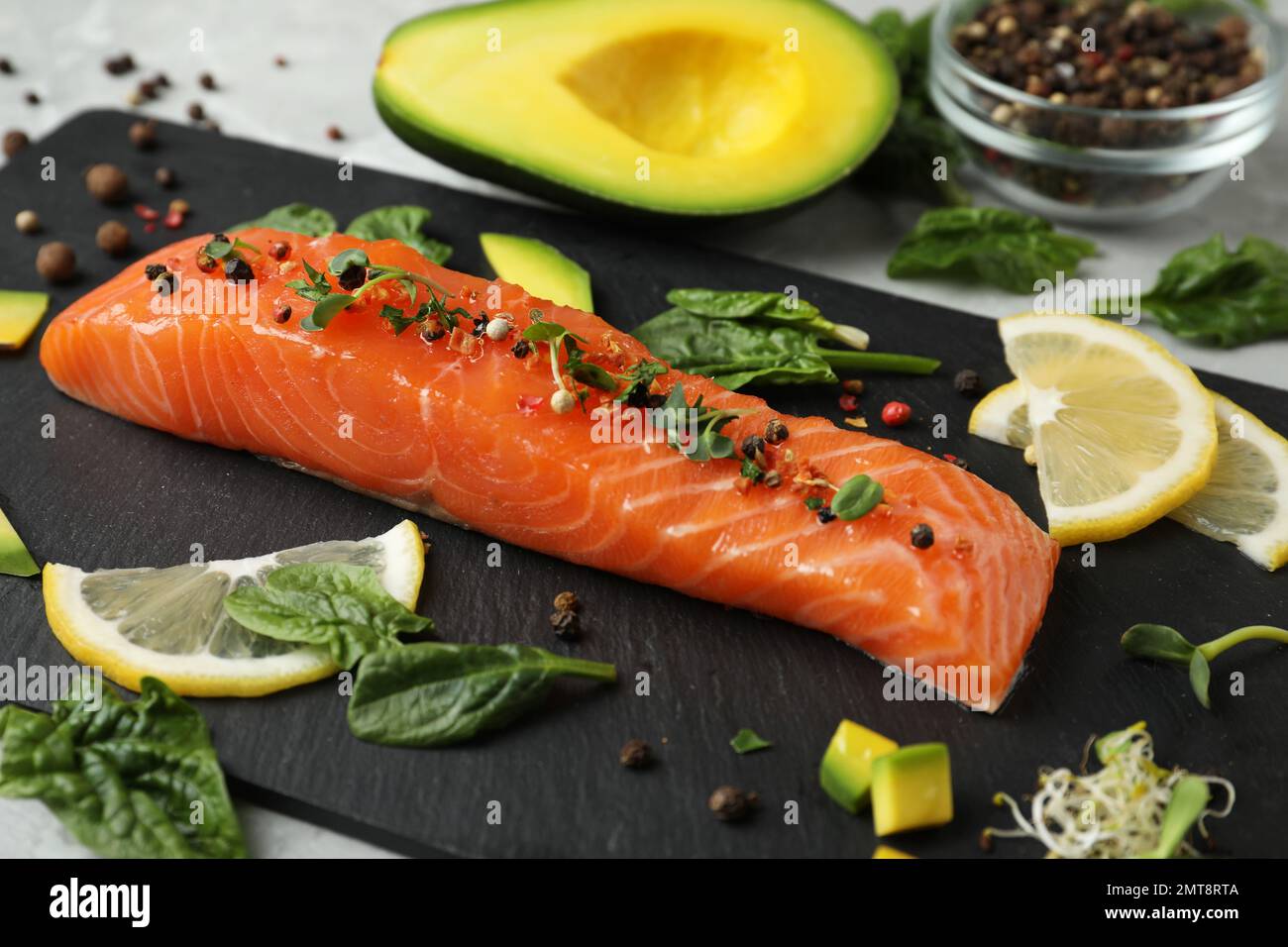 Delicious salmon served with spinach, lemon and avocado on slate board ...