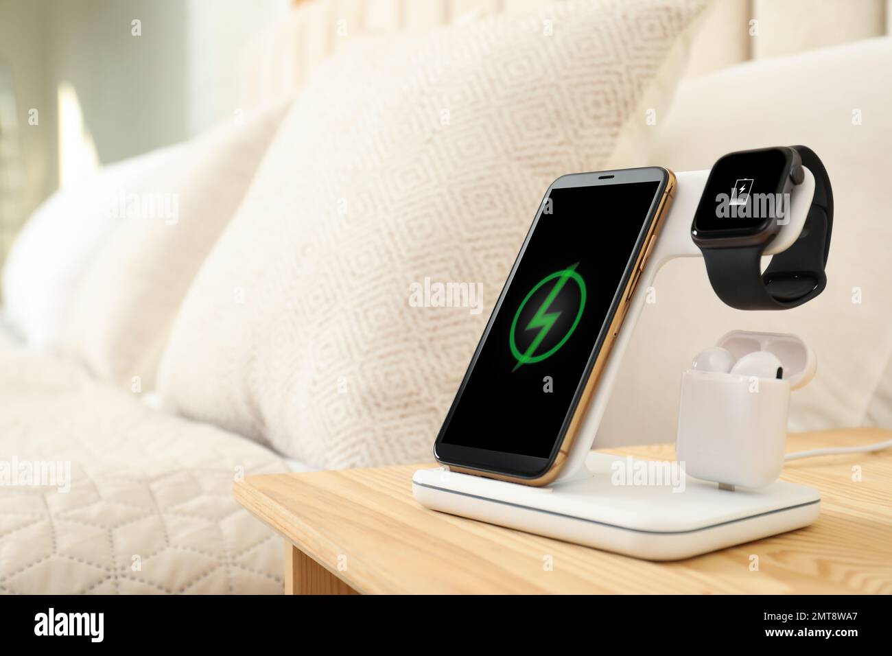 Different gadgets charging on wireless pad in bedroom. Space for text ...