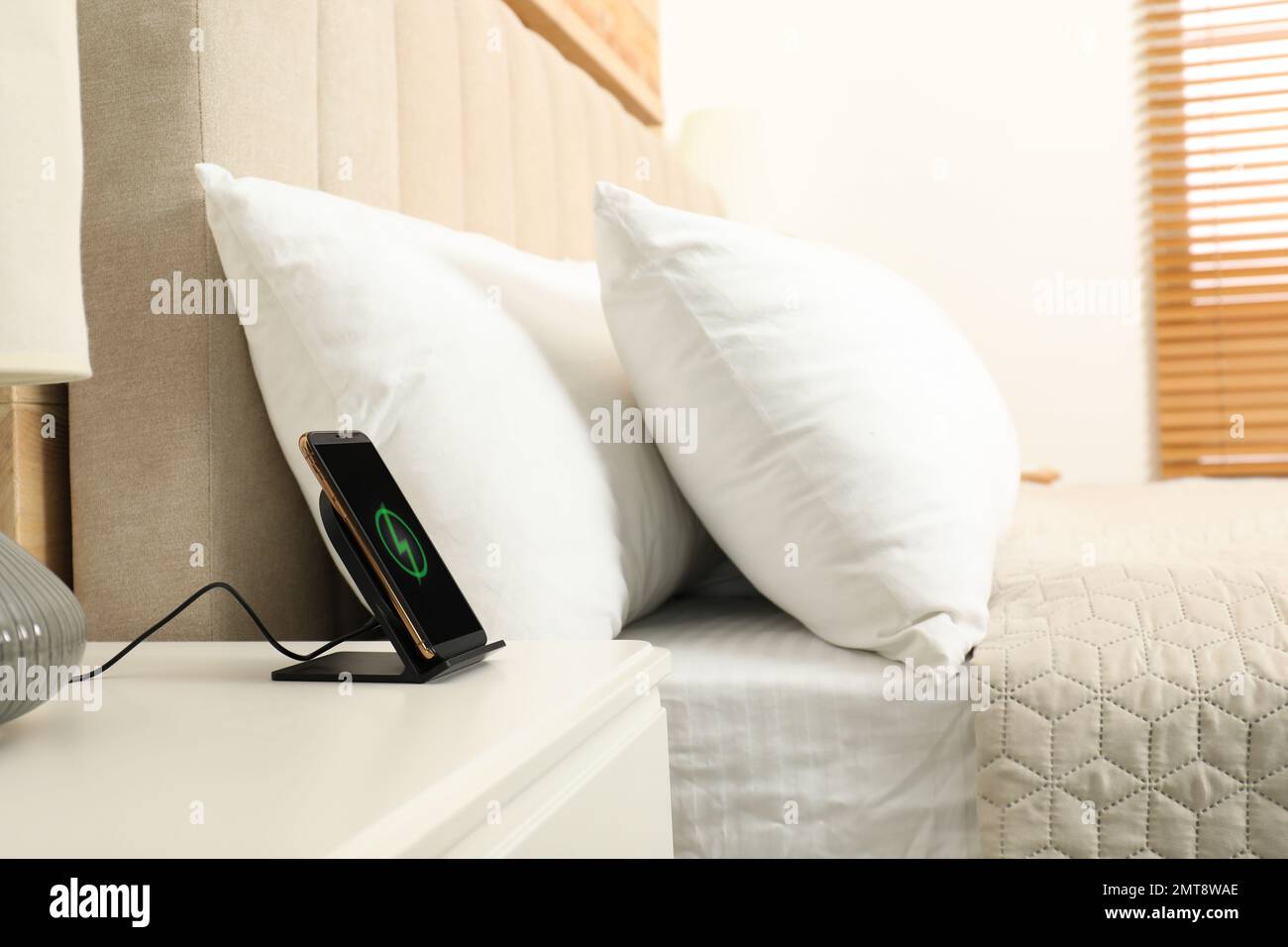 Modern mobile phone charging on wireless pad in bedroom Stock Photo - Alamy