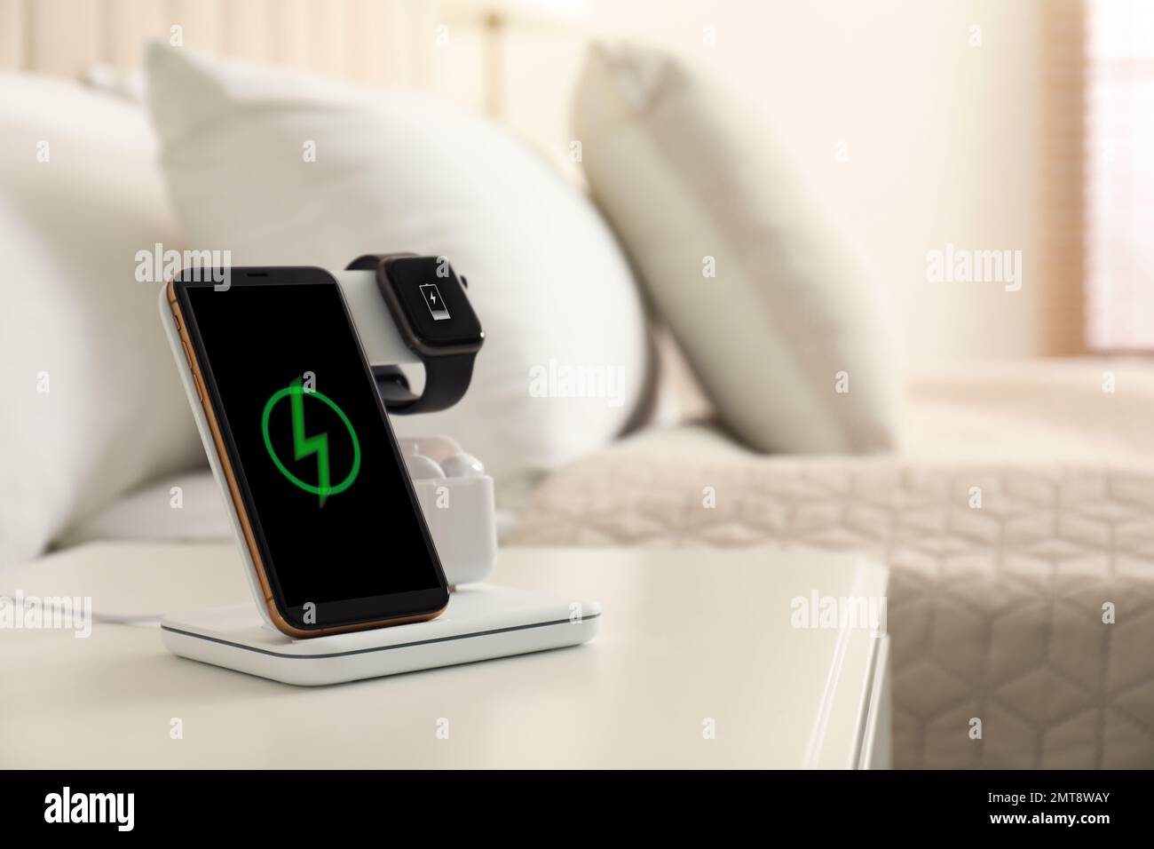 Different gadgets charging on wireless pad in bedroom. Space for text ...