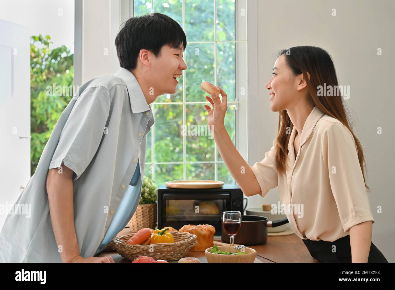 Lovely young woman feeding his boyfriends with donut while cooking in ...