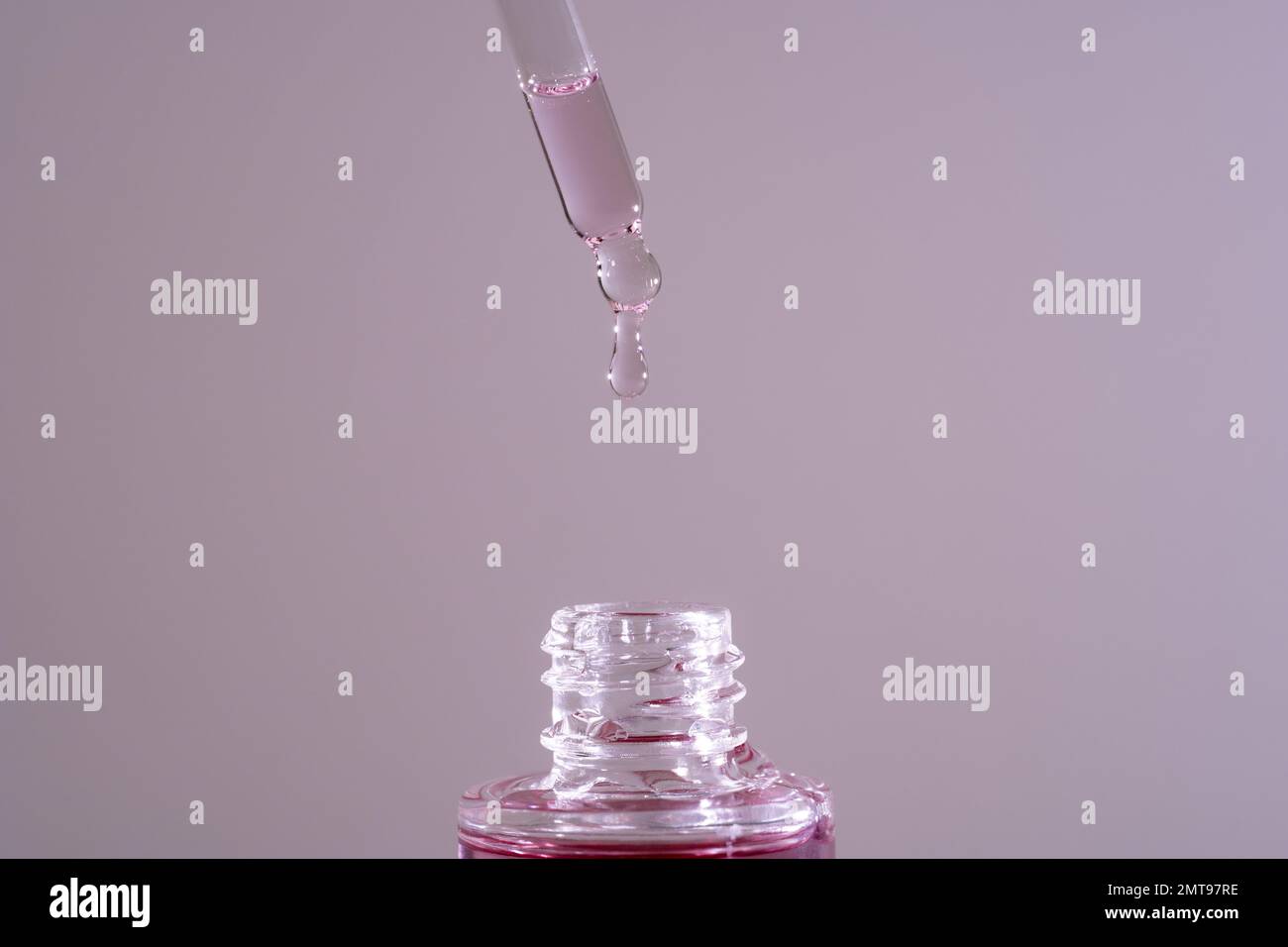 Pink face oil drop from glass pipette dropper. Macro close up for ...