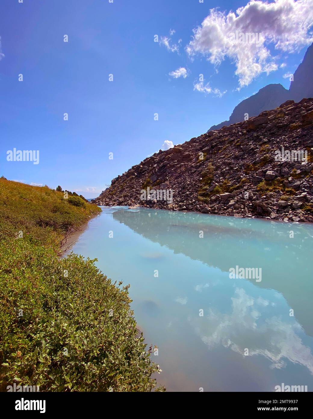 Turquoise milky water of the Karakabak River among the stones and grass ...