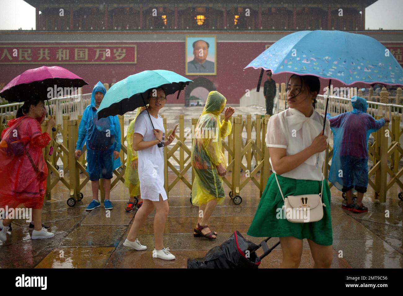 Visitors carrying umbrellas or wearing rain ponchos walk past a large ...