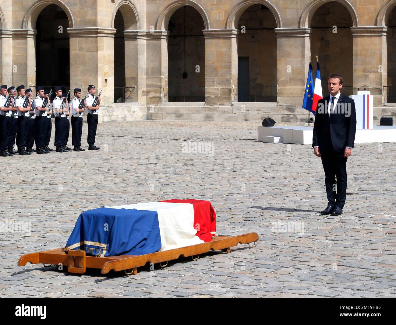 French President Emmanuel Macron stands in front of the flag-draped ...