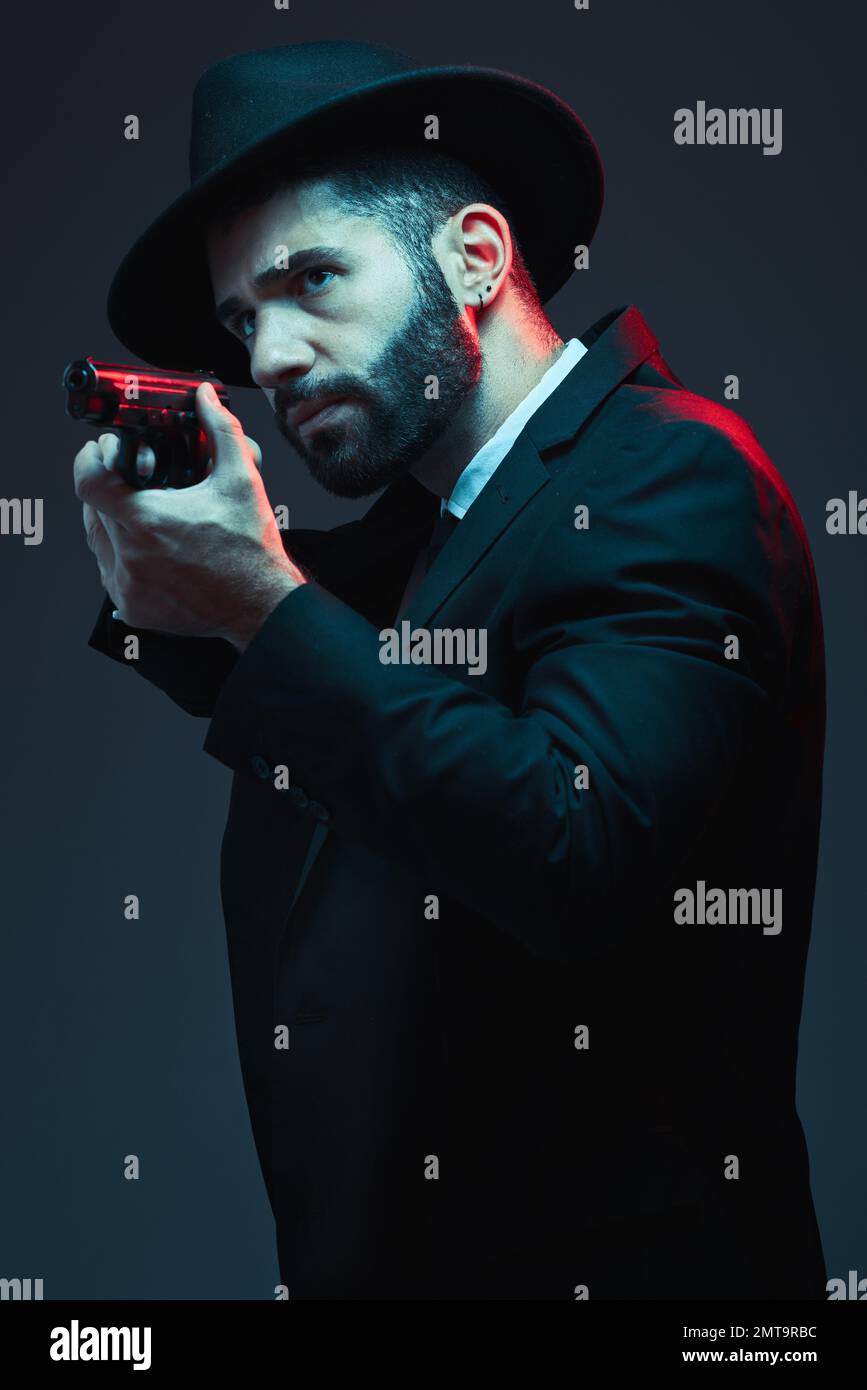 Gangster, suit and shooting gun on dark studio background in secret spy ...