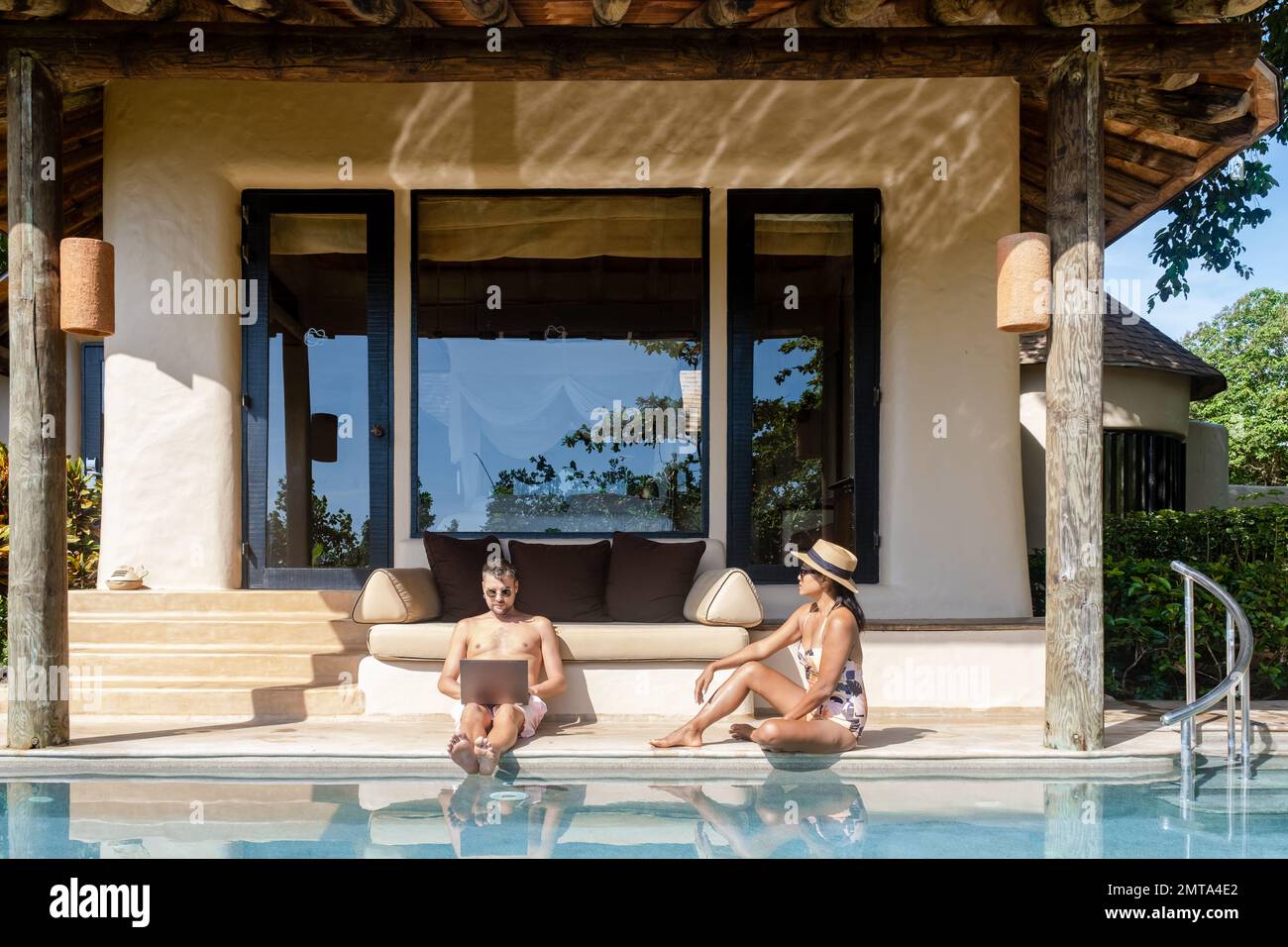 Men working at a laptop a digital nomad working at a swimming pool during a vacation on a ...