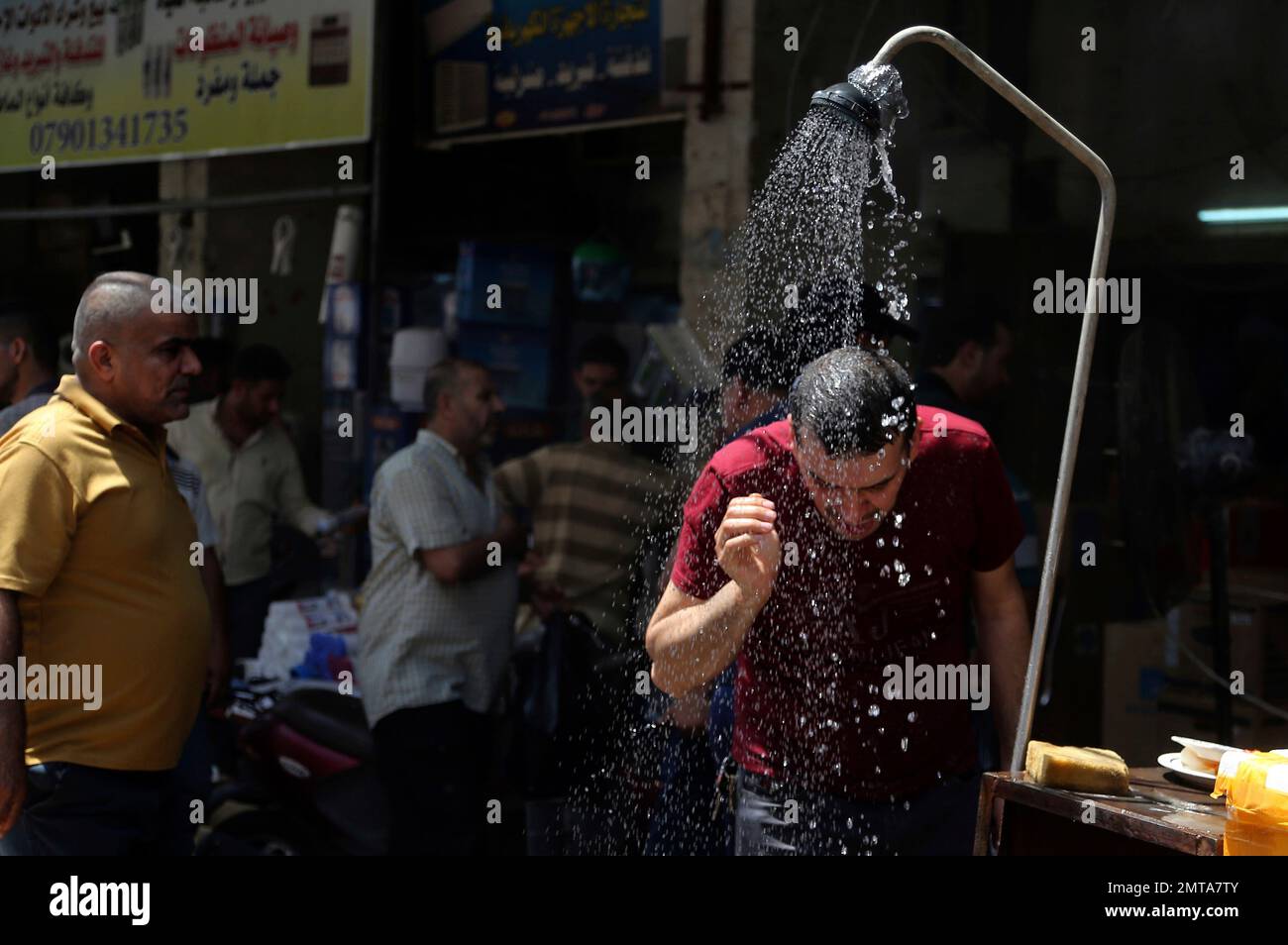 An Iraqi man uses an open air shower to cool off from the summer heat ...