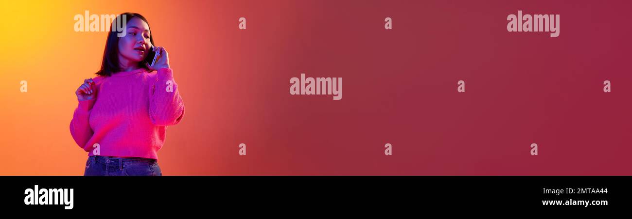 Young girl in pink sweater talking on phone over gradient orange ...