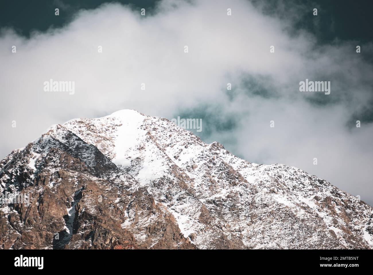 The top of a triangular rocky mountain is covered with snow against the ...