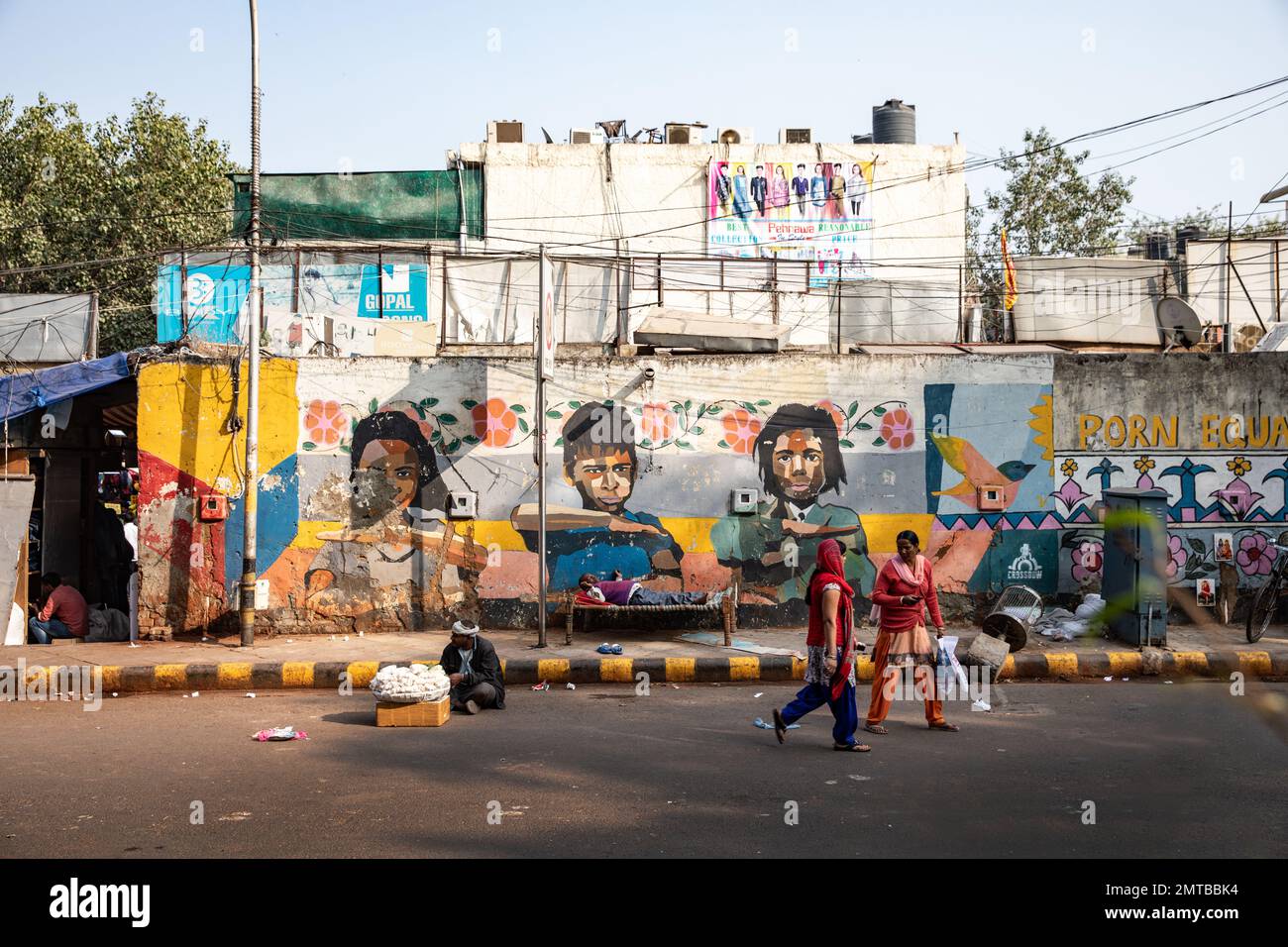 A man taking a nap while two women pass by in a colourful street in in ...