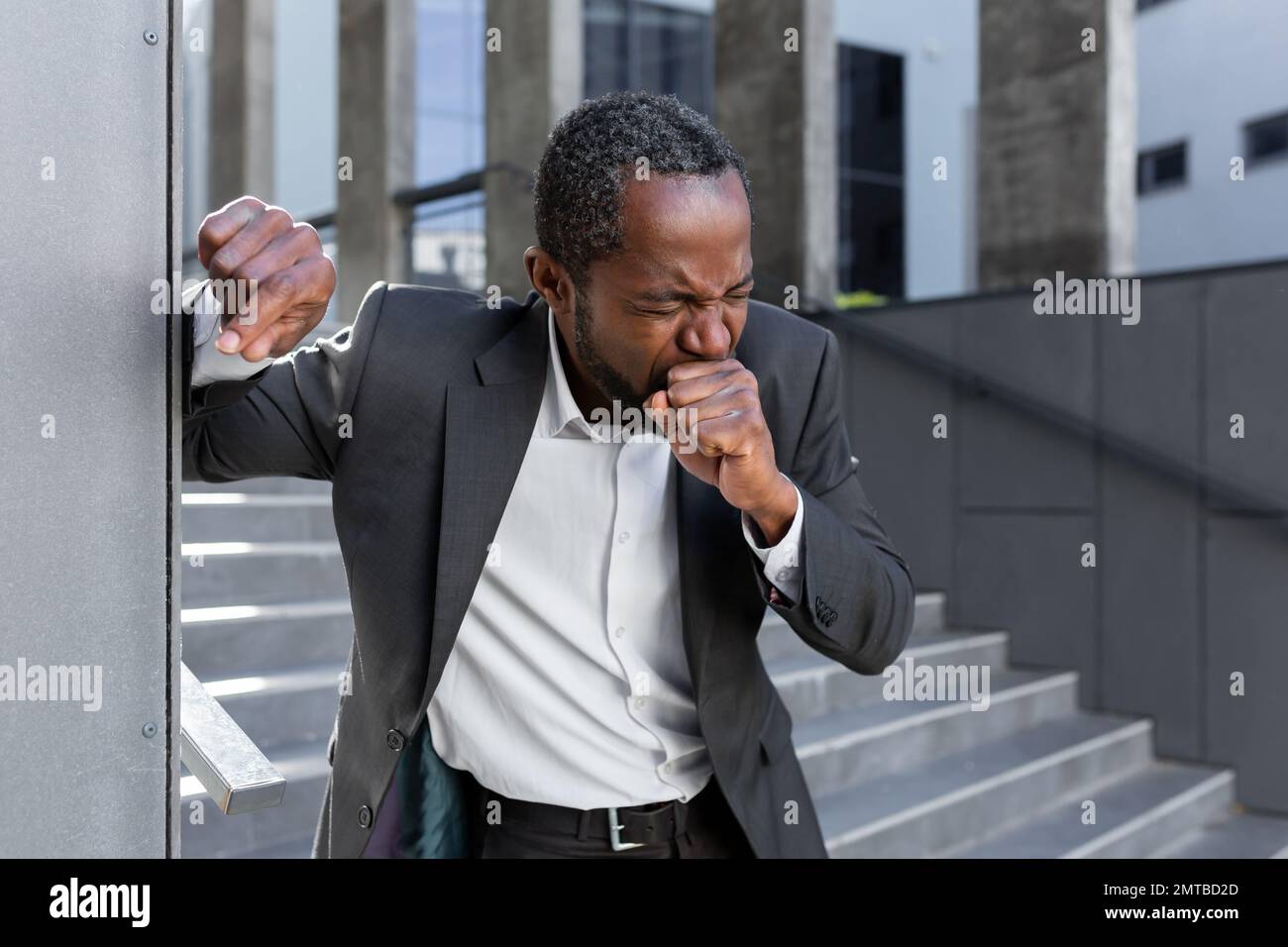 Cough attack. An African-American businessman in a suit is holding on ...
