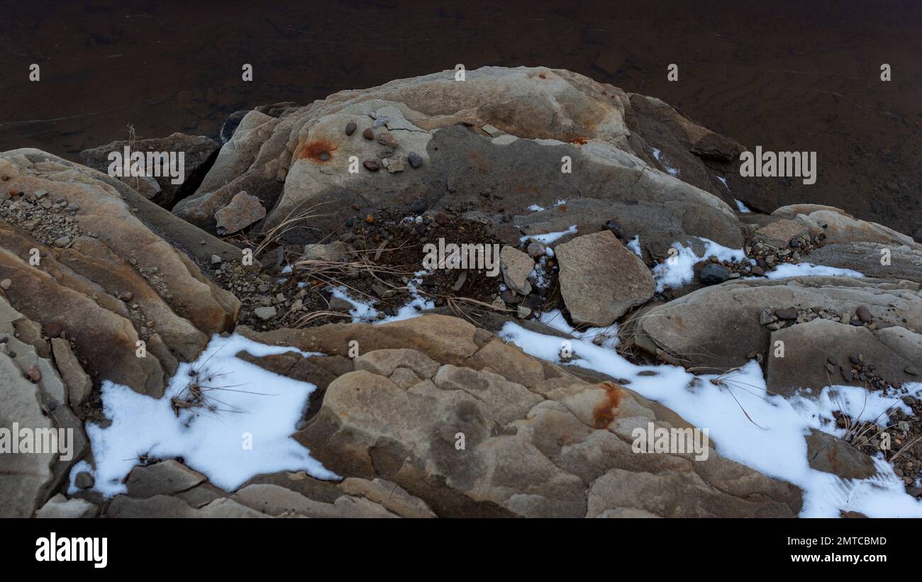 Photo of a rock outcrop on the shore with dark water with snow and ...