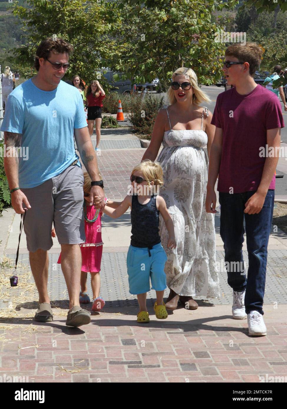 A heavily pregnant Tori Spelling in a long lose fitting white dress and ...
