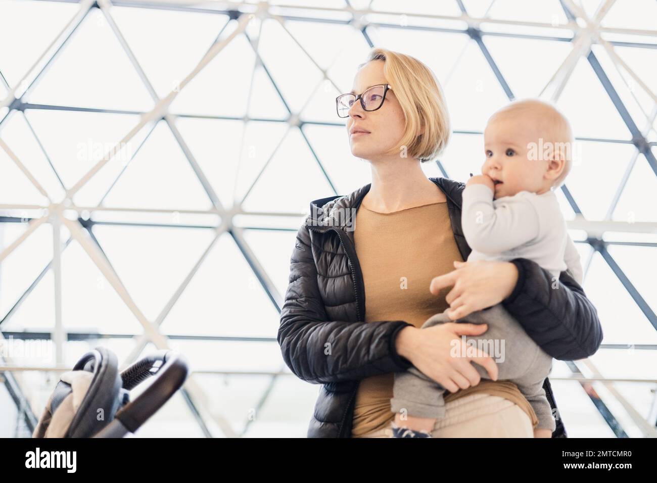 Mother carying his infant baby boy child, pushing stroller at airport ...