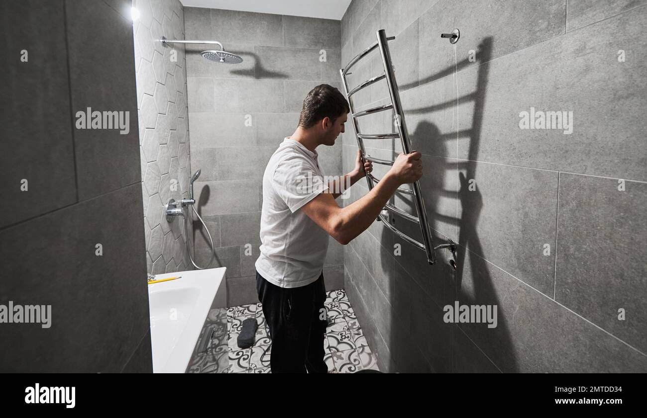 Male plumber hanging electric towel rack dryer on the wall in bathroom ...