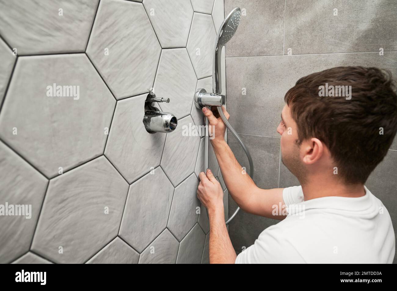 Male worker fixing metal bath showerhead and doing plumbing works while ...