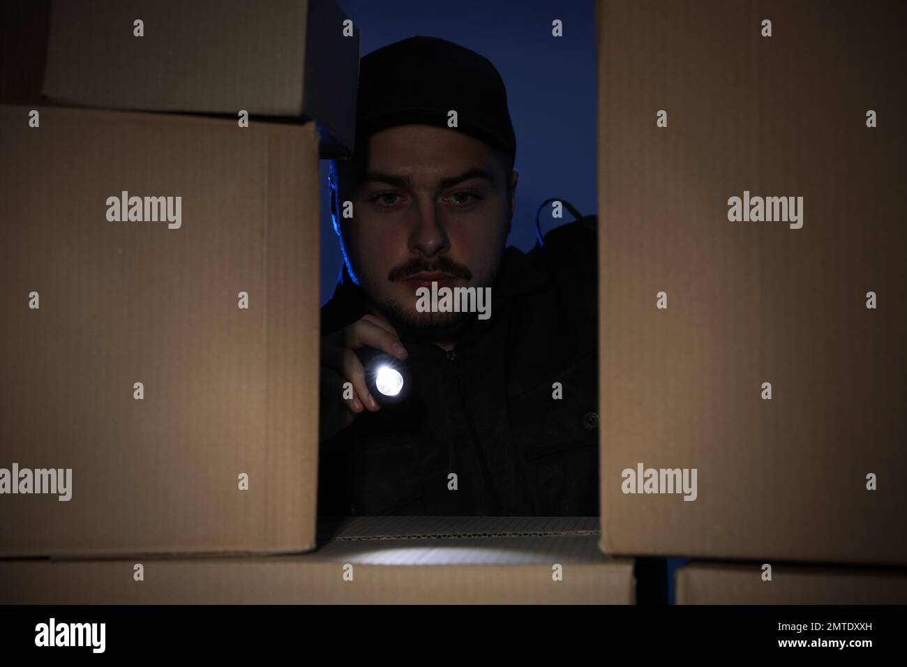 Security guard with flashlight looking through pile of cardboard boxes ...