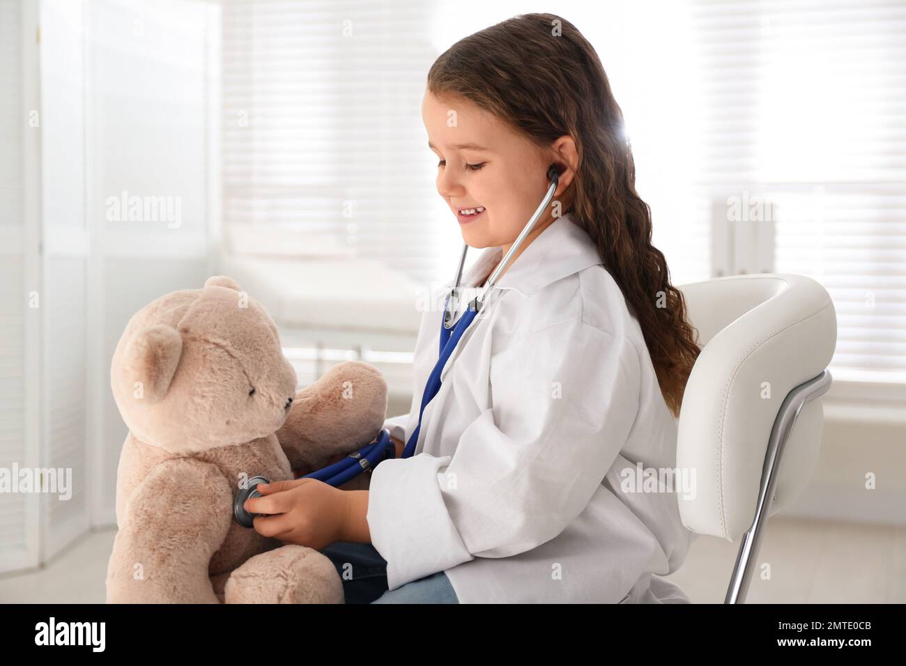 Cute little girl playing doctor with teddy bear in clinic Stock Photo ...